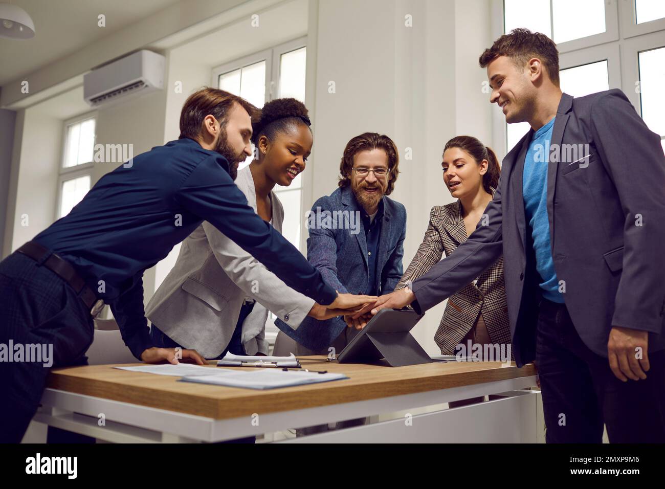 Joyful male and female colleagues make stack of hands together as ...