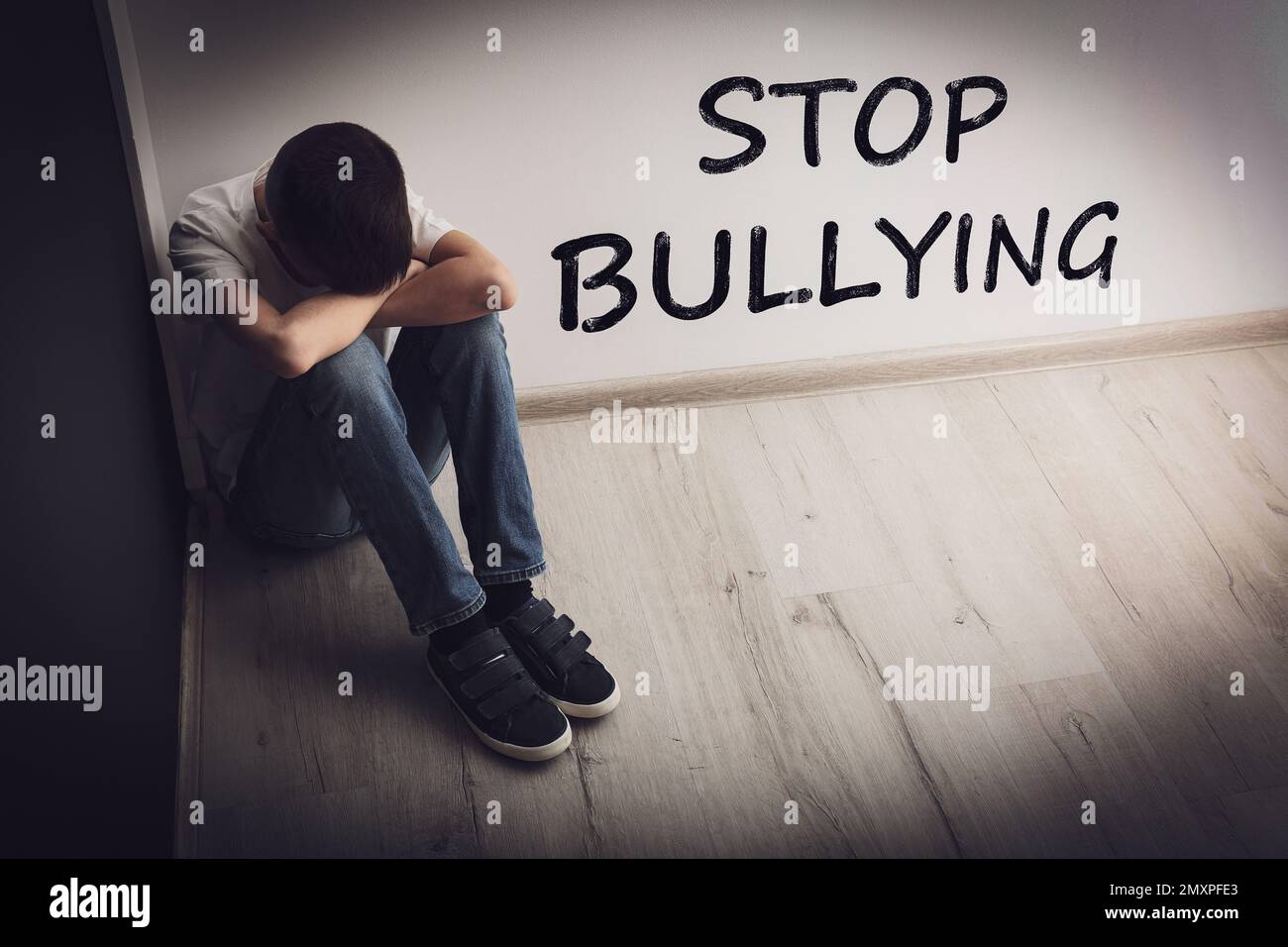 Message STOP BULLYING and upset boy sitting on floor indoors Stock ...