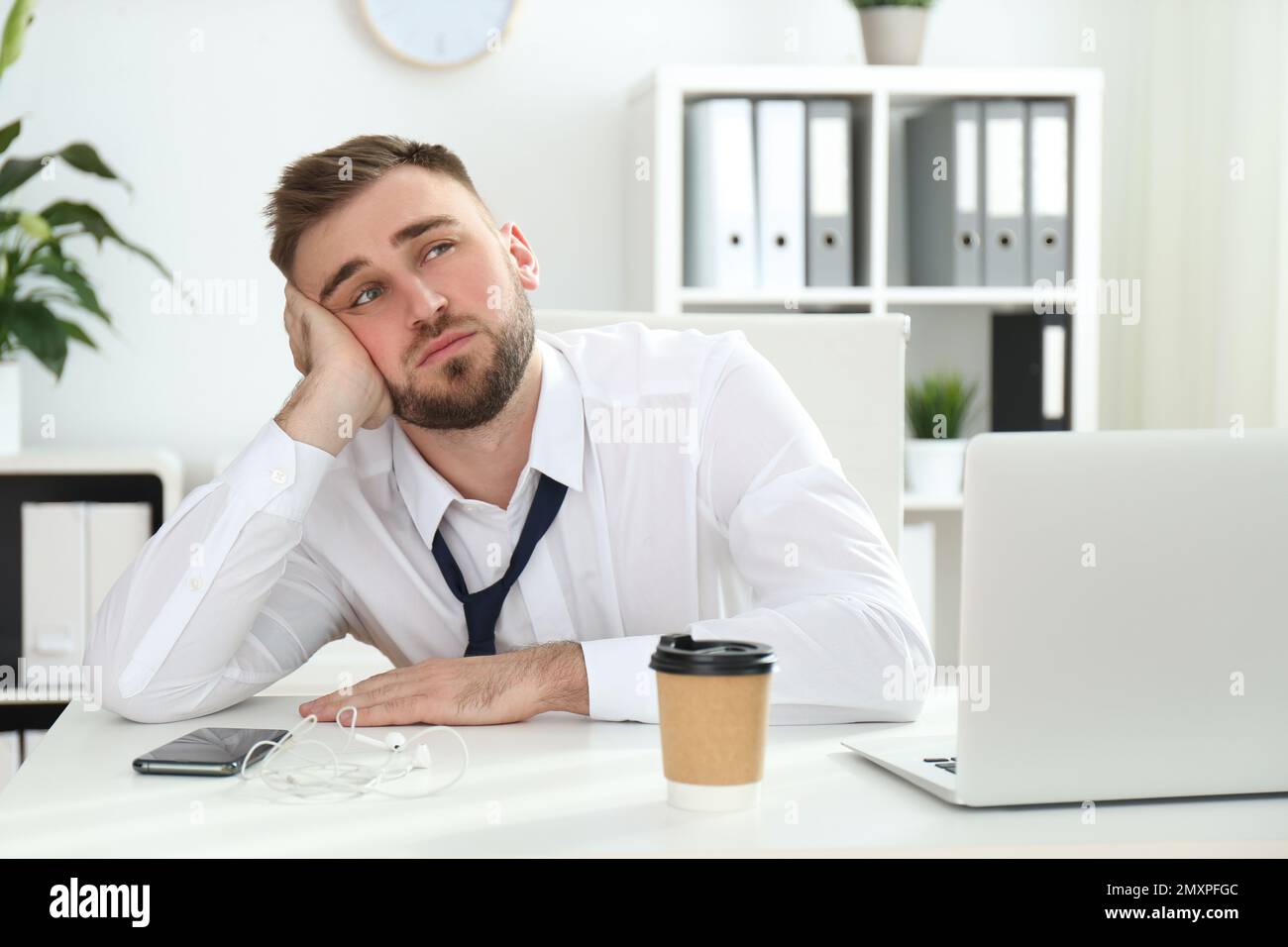 Lazy young man wasting time at table in office Stock Photo - Alamy