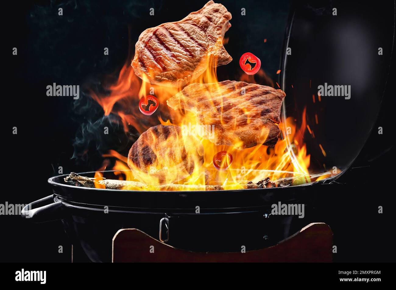 Meat and chili pepper slices falling onto barbecue grill with flame ...