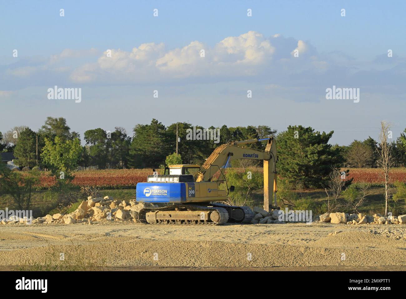 A KAMATSU EXCAVATOR moving rocks with tree's and blue sky at a ...