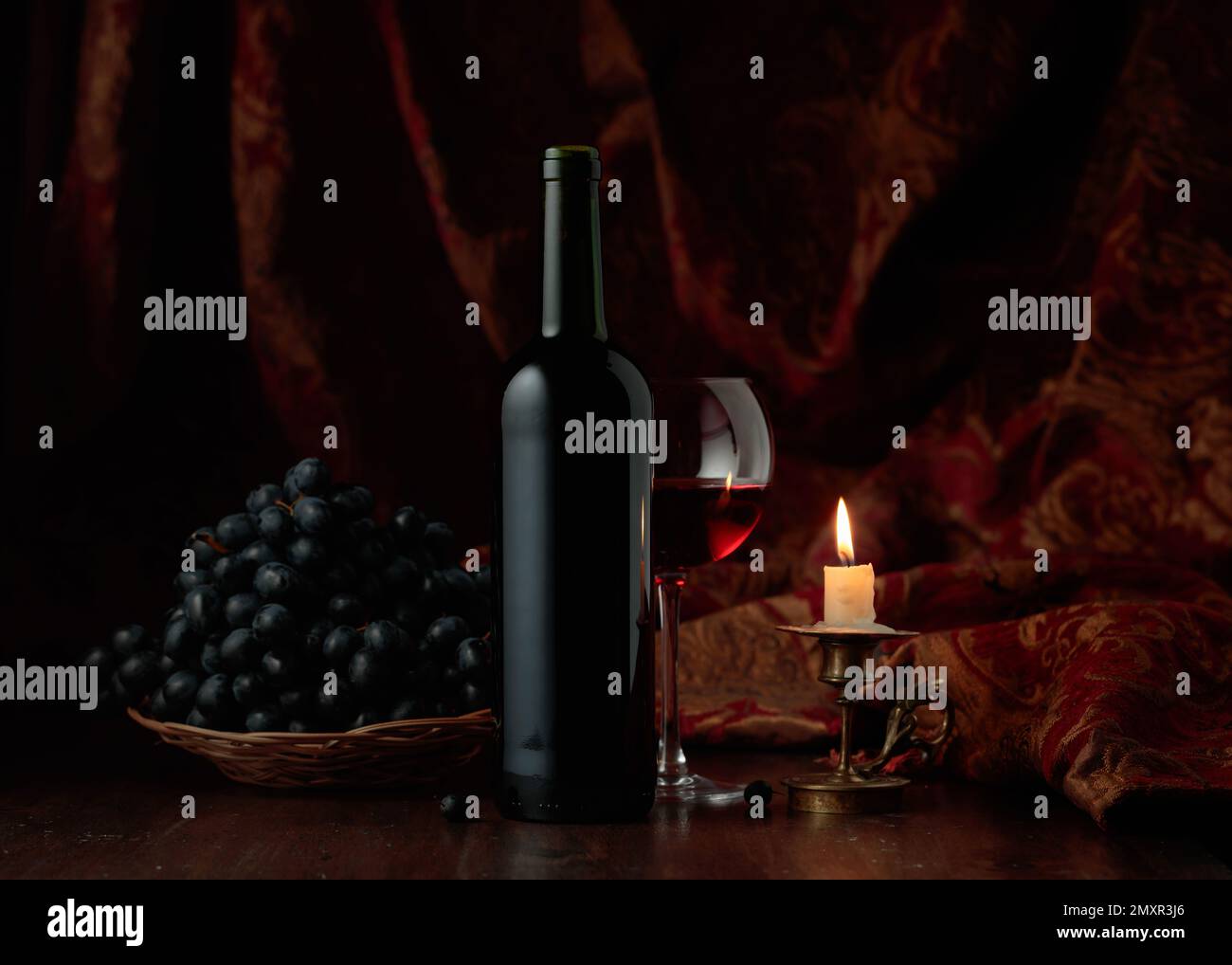 Still life with red wine, grapes, and a burning candle in an old brass ...