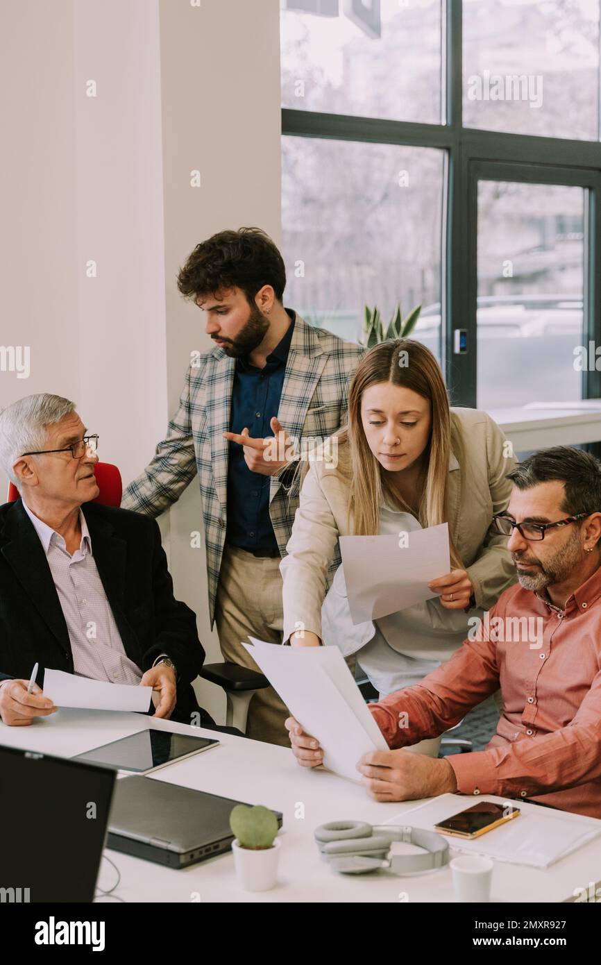 A senior businessman is getting help by his blonde female coworker while their colleagues are ...