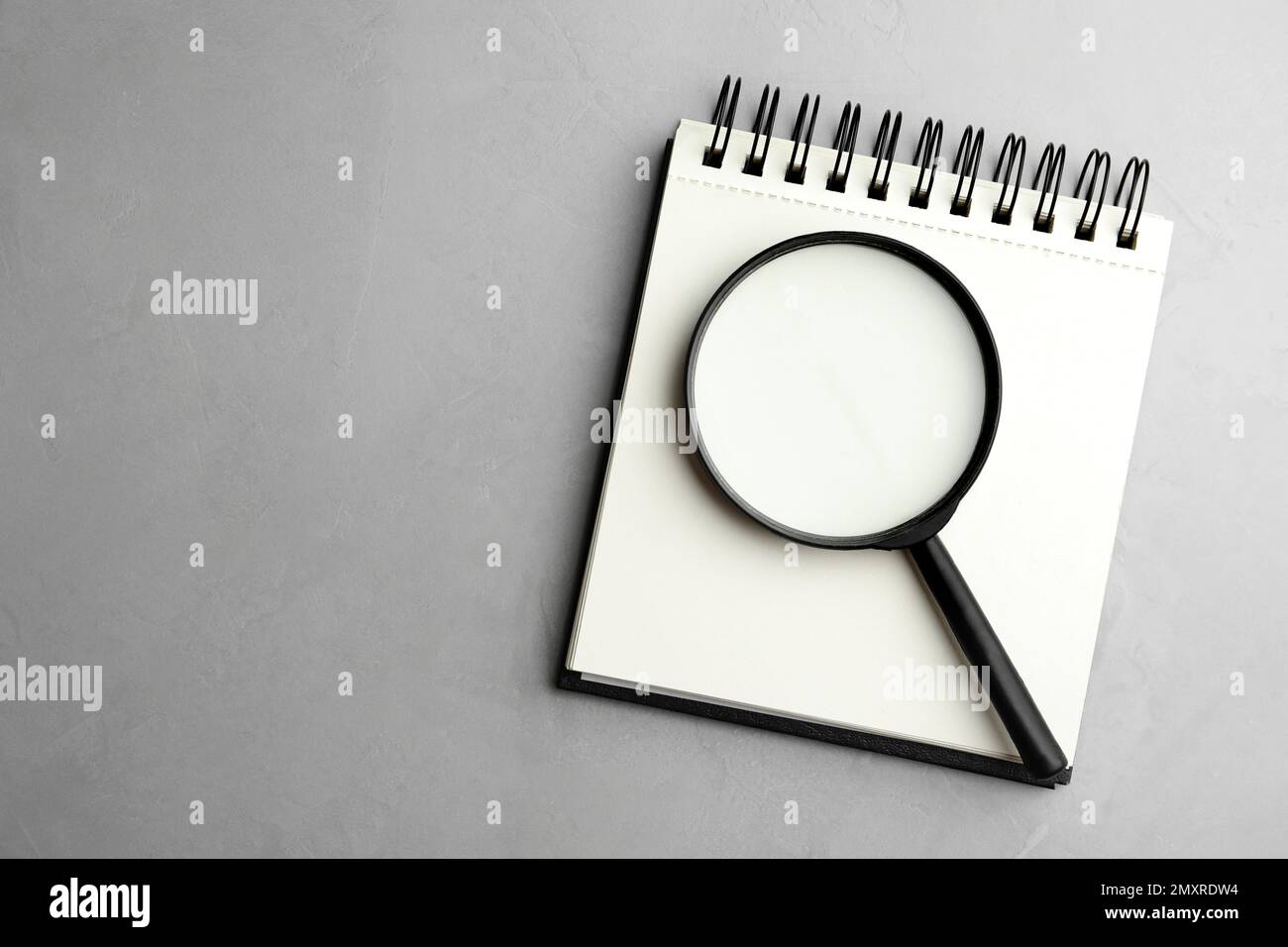 Top view of magnifier glass and empty notebook on light grey stone ...