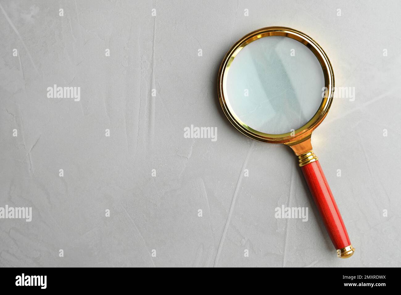 Top view of magnifier glass on light grey stone background, space for ...