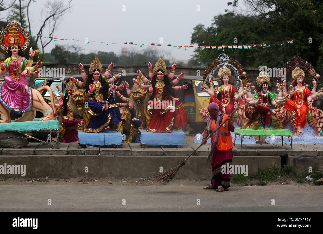 An Indian municipal worker sweeps a street in front of idols of Hindu ...