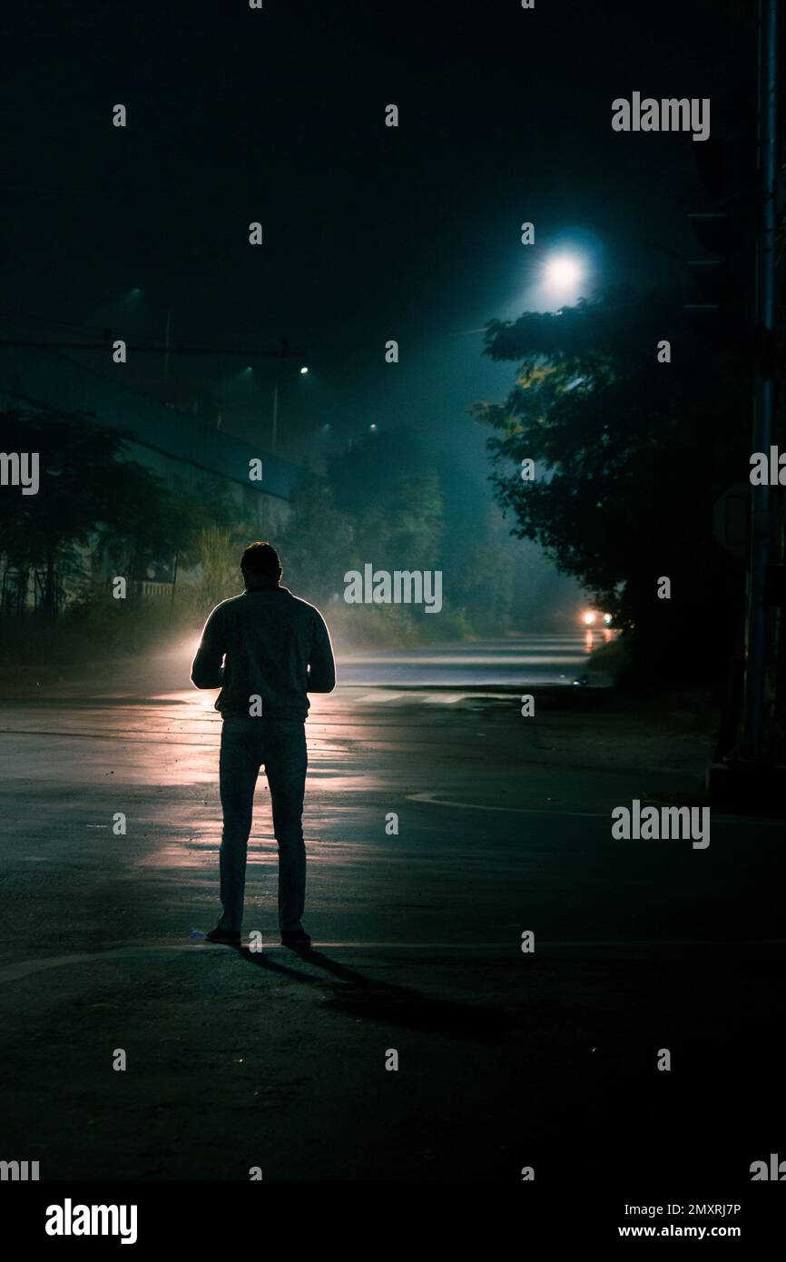 A vertical shot of man walking at night on street corner in rural ...