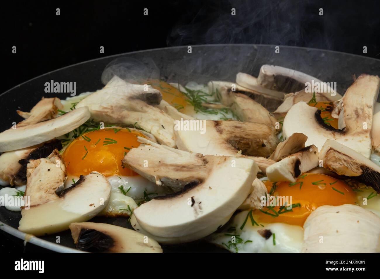 Fried mushrooms and eggs in a pan. The process of cooking breakfast ...