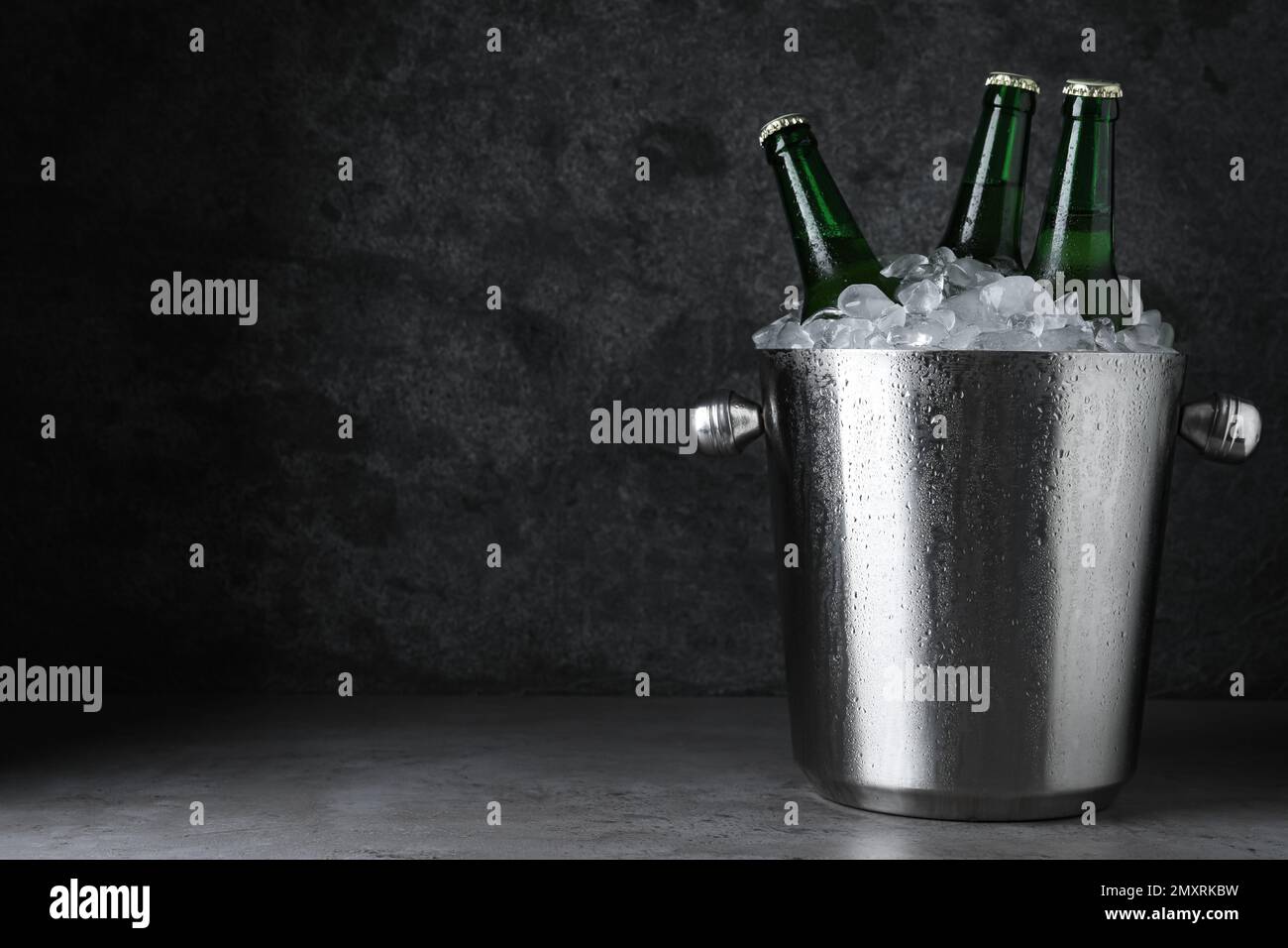 Metal bucket with beer and ice cubes on grey table. Space for text ...