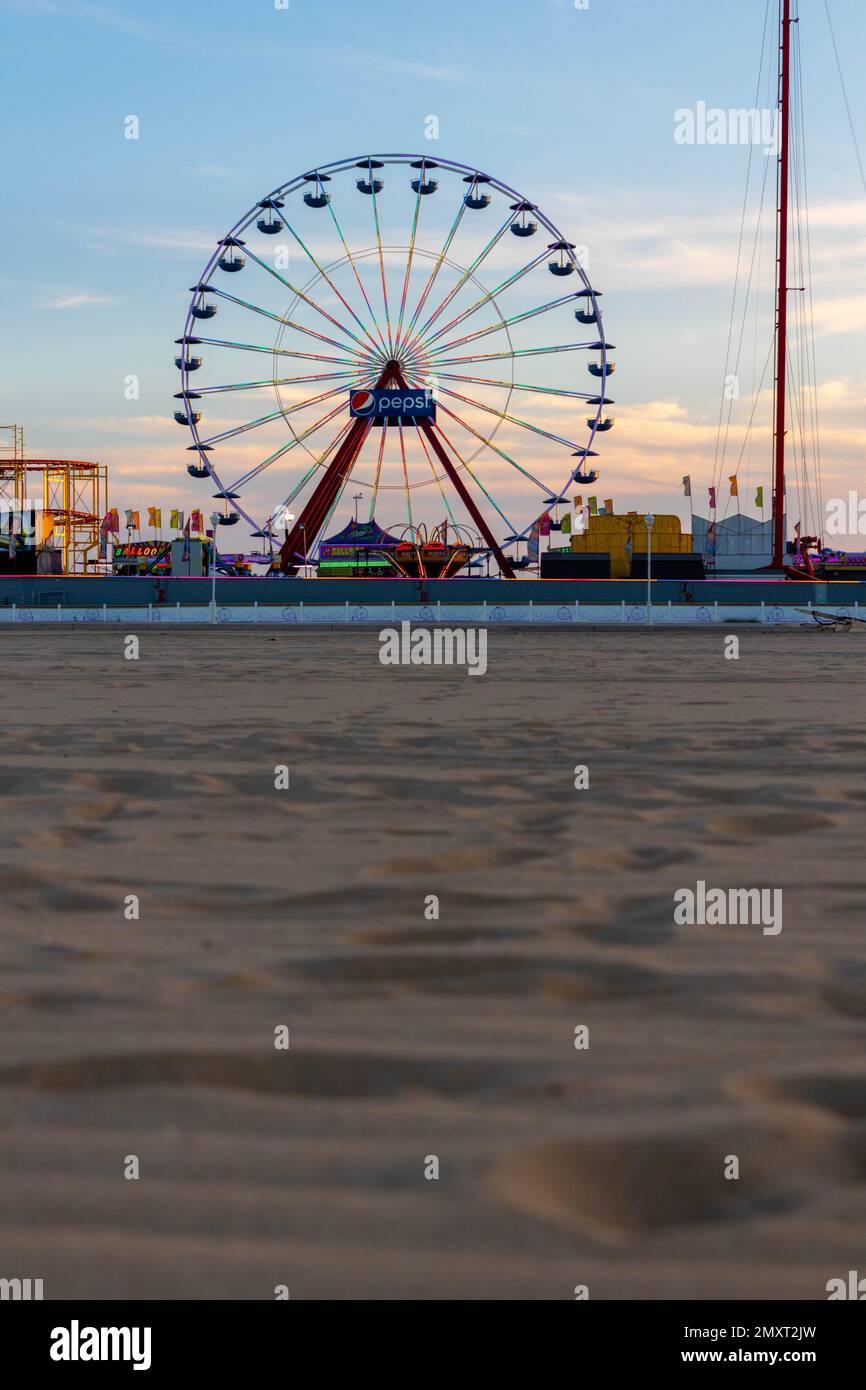 A vertical shot of the sandy beach with a Ferris wheel of the amusement ...