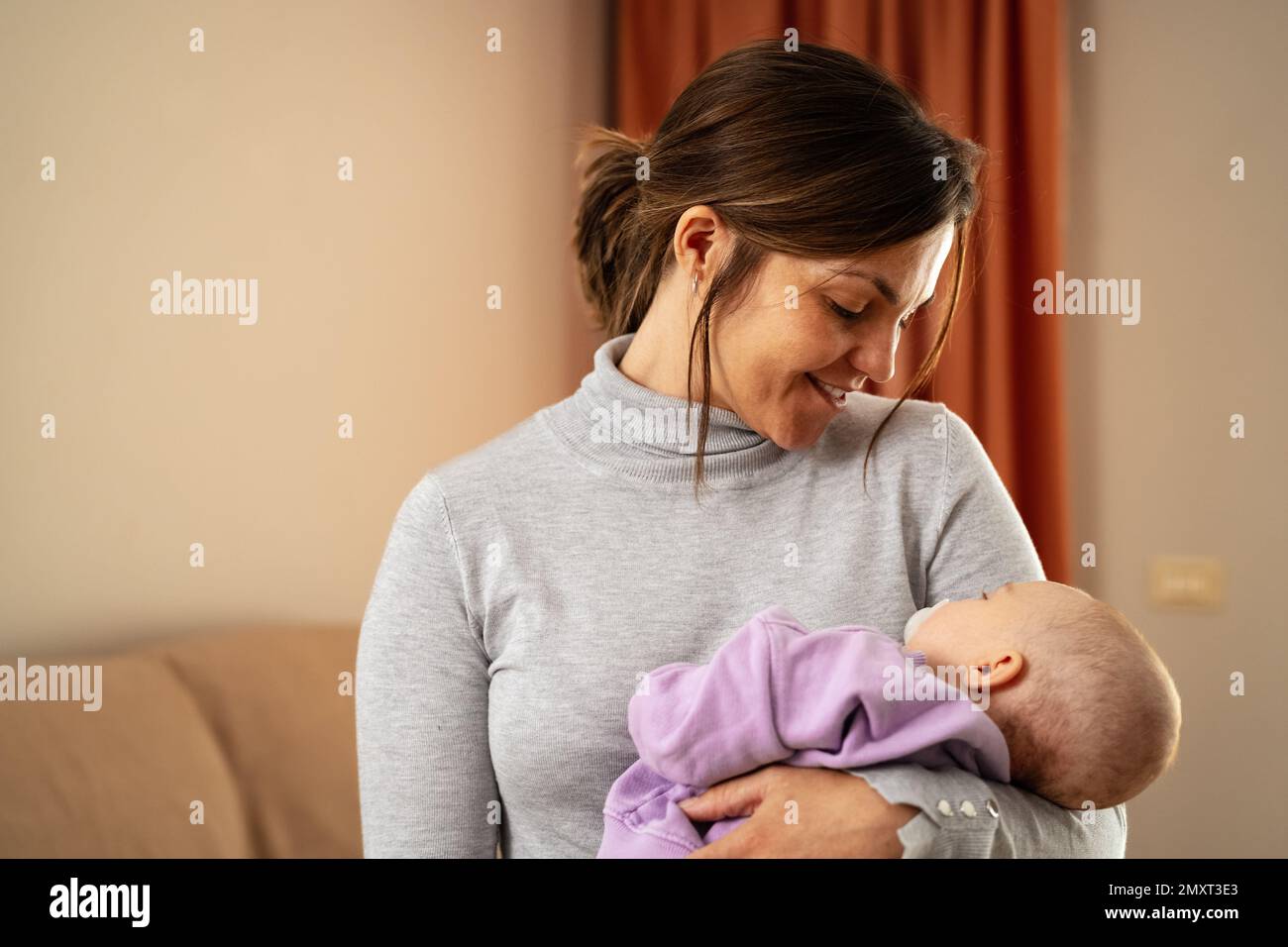 Happy mother taking care of her small baby sleeping in her arms at home - Concept family and ...