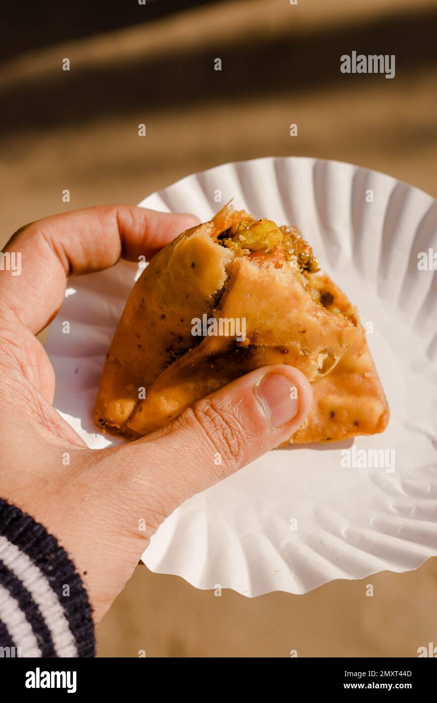 A vertical closeup of a person holding a Samosa, appetizing Indian ...