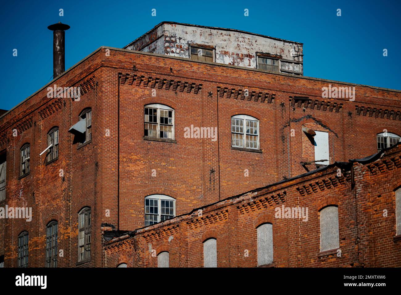 An old run down factory with broken windows against a clear blue sky ...