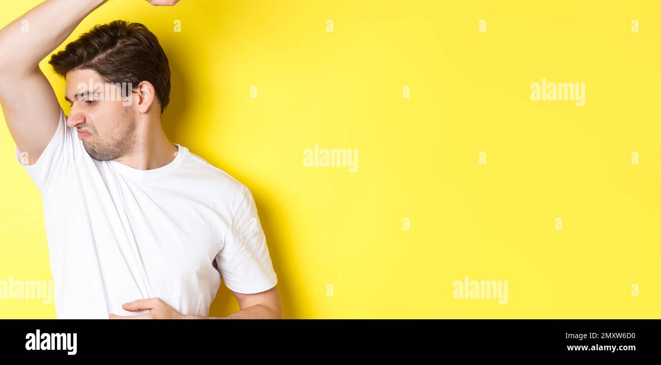 Man in sweat smelling his armpit, standing in white t-shirt and ...