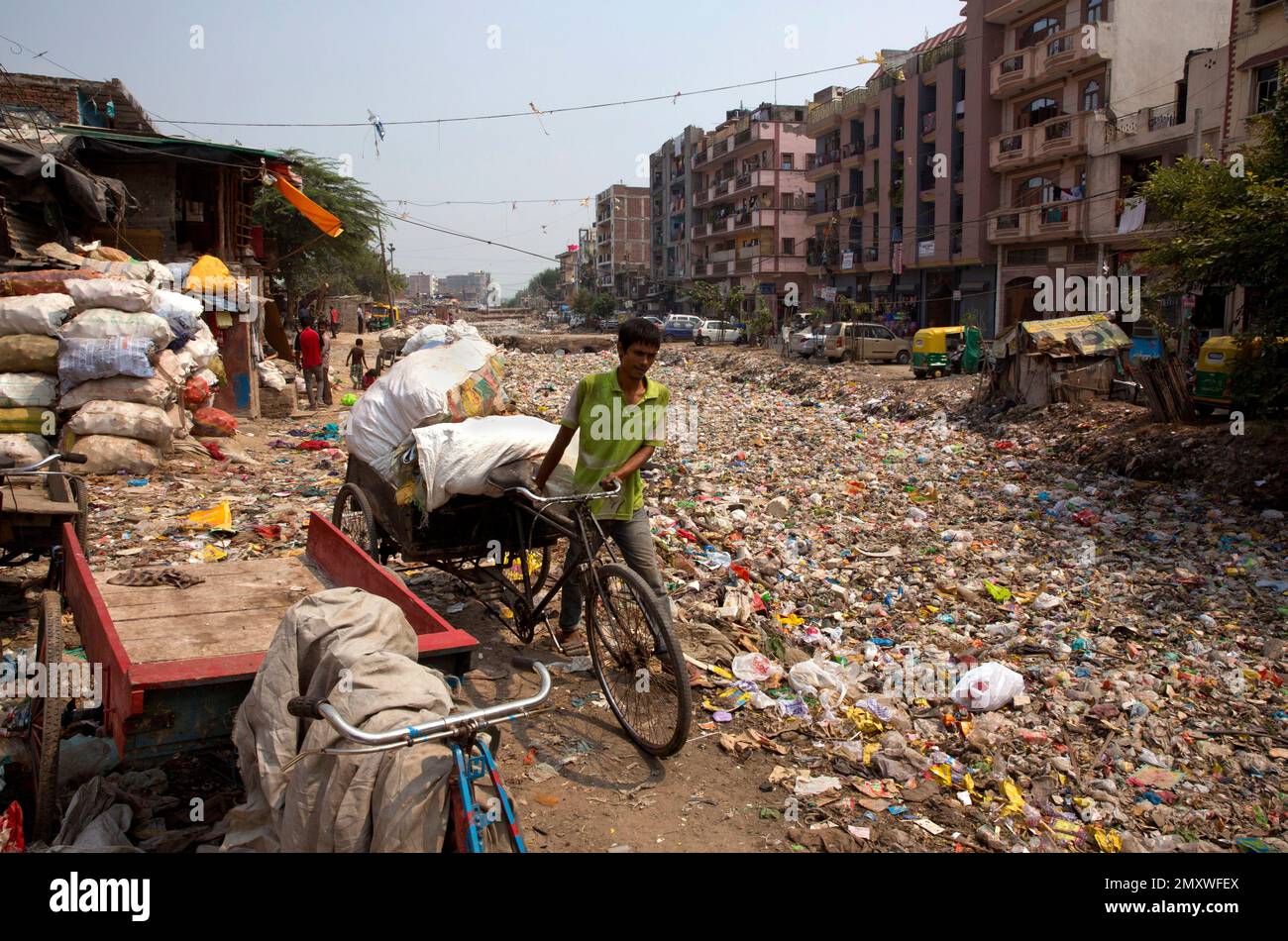 A rag picker pulls his rickshaw along an open drain filled with plastic ...