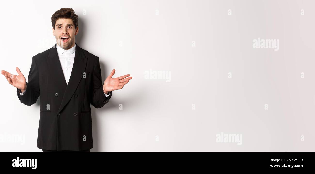 Portrait of confused and worried handsome man in suit, looking at ...