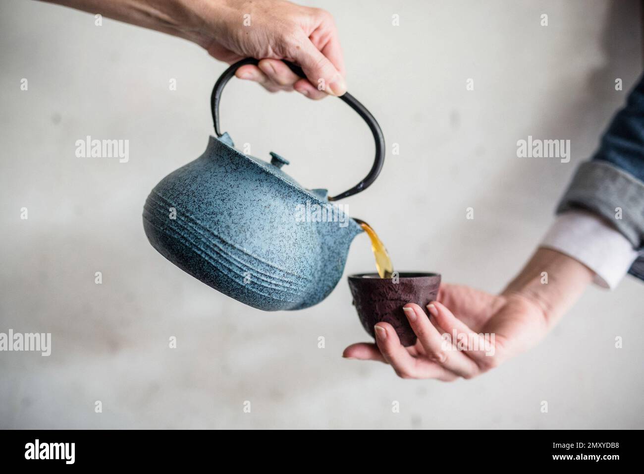 A hand holding a blue teapot pouring out tea into a cup in another ...