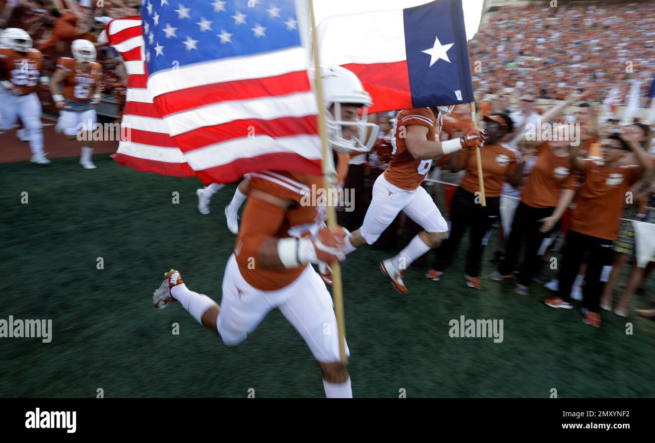 Texas players carry flags as they lead their team on to the field ...