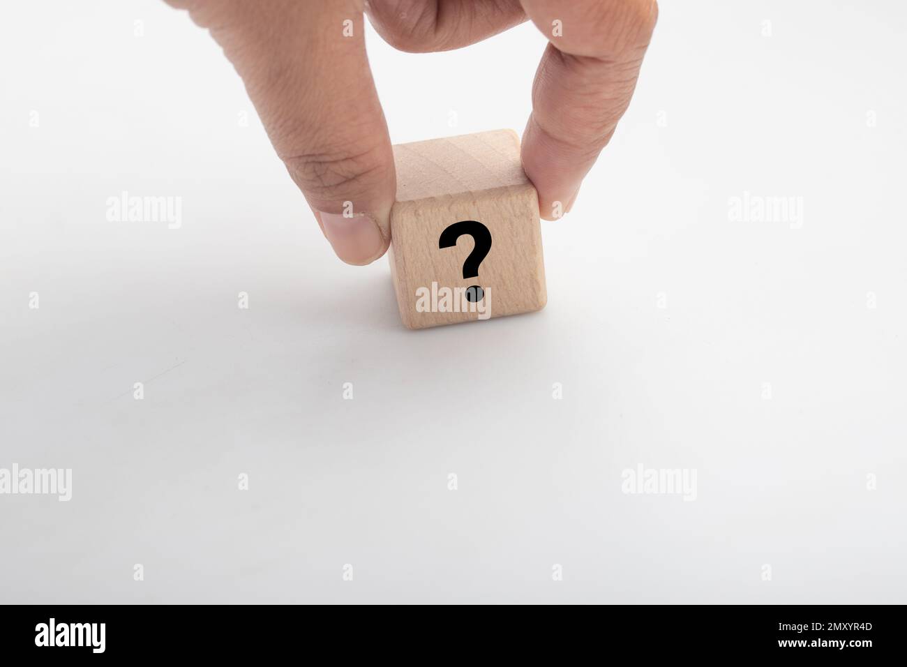 Hand holding a wooden block with a question mark on a white background ...