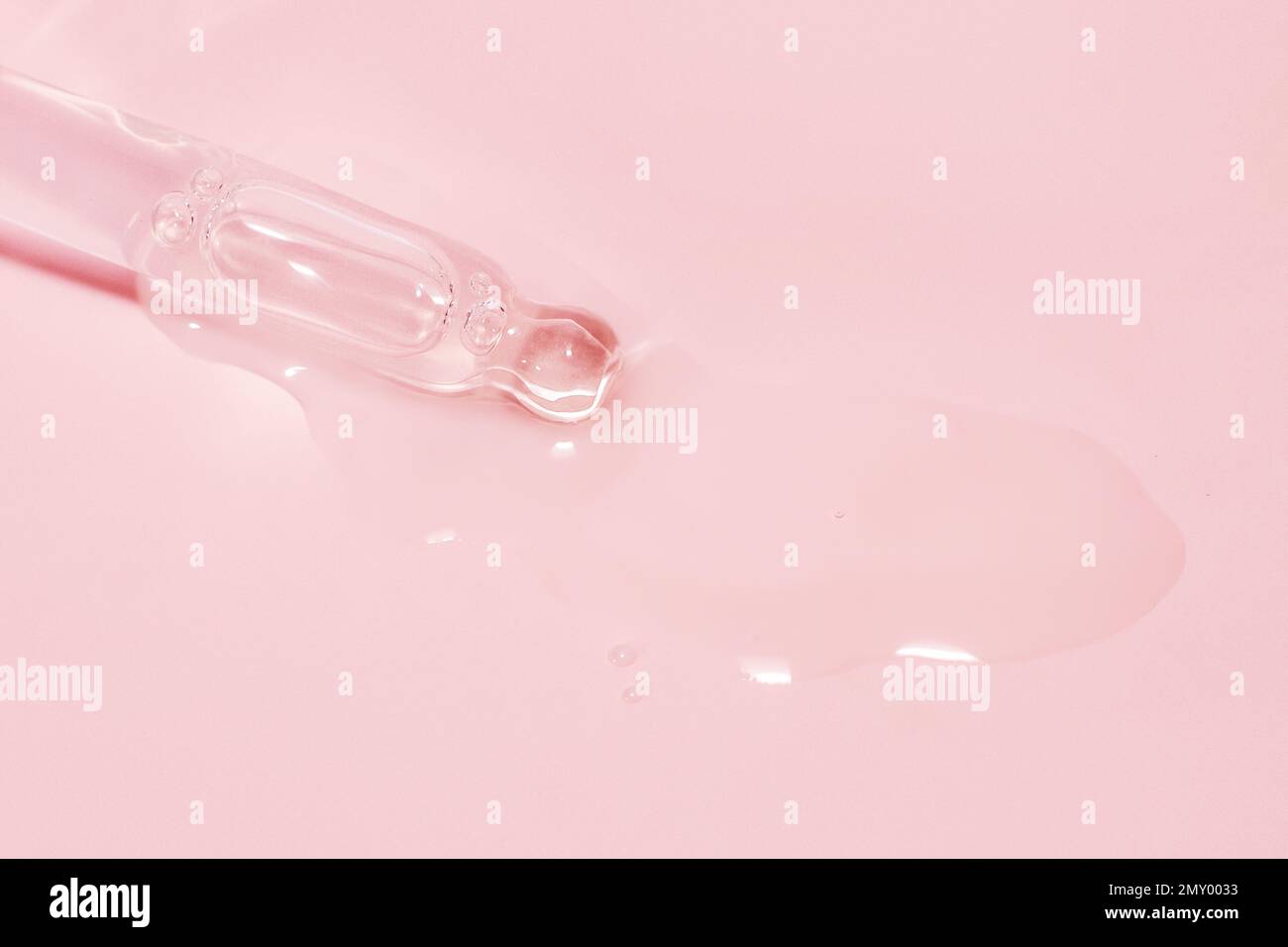 Cosmetic pipette with dripping liquid and drops on a pink background ...
