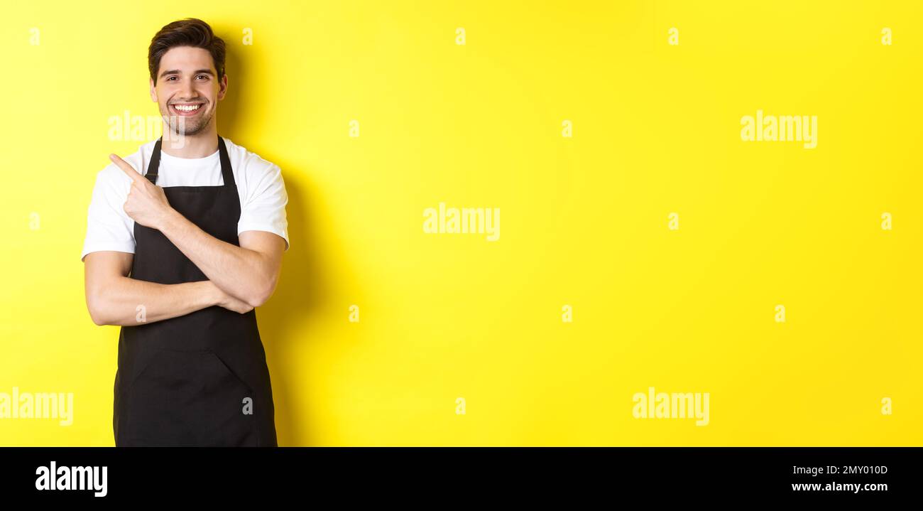 Happy barista pointing finger left and smiling, wearing black apron ...