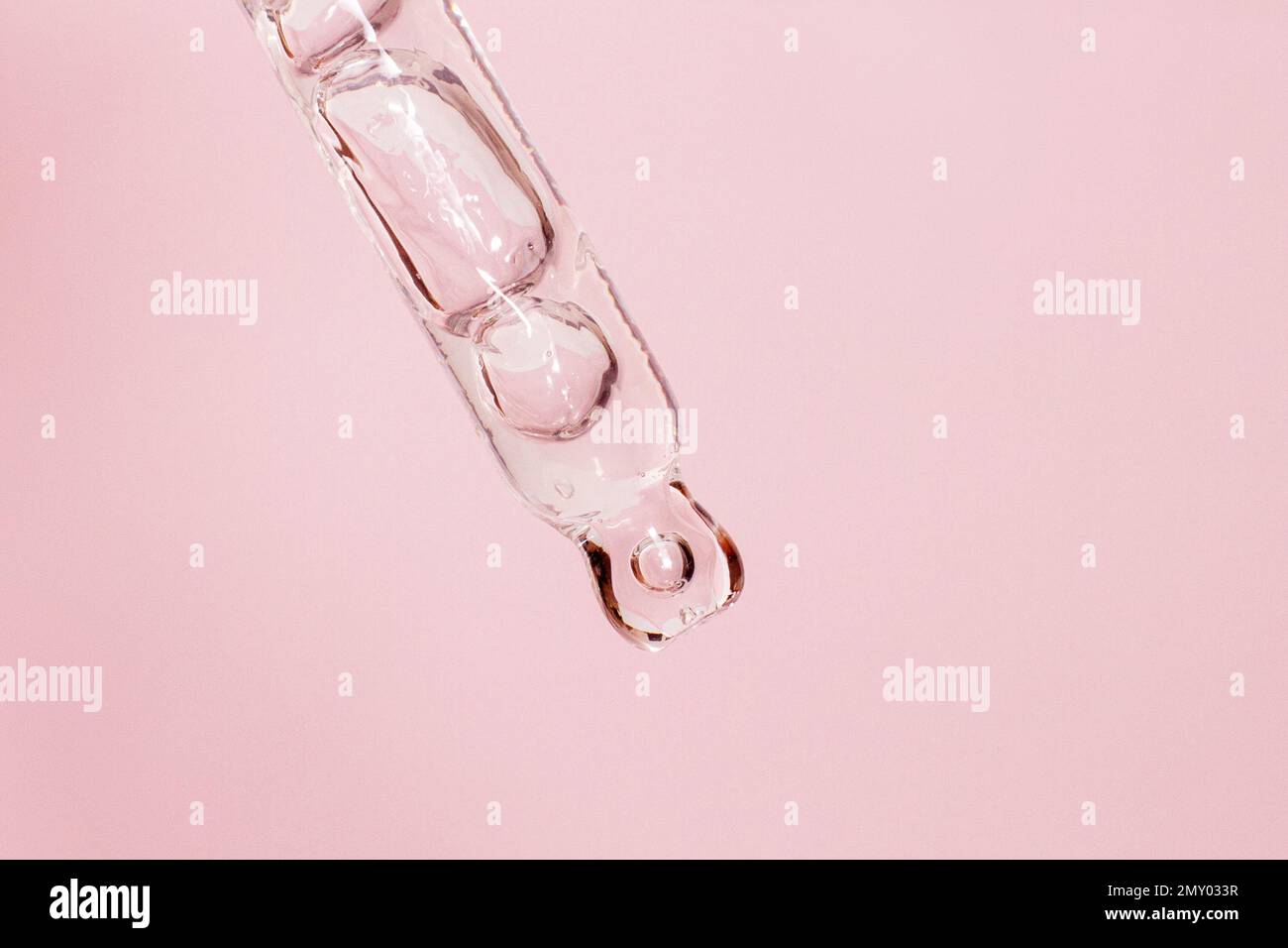 Cosmetic pipette with dripping liquid and drops on a pink background ...
