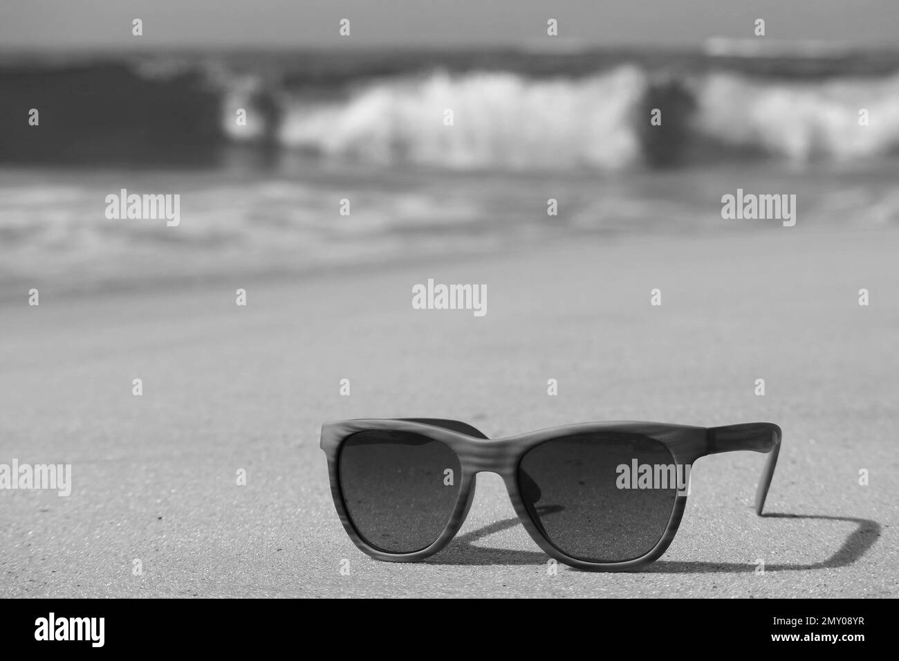 Monotone sunglasses on the sandy beach with blurry splashing waves in ...