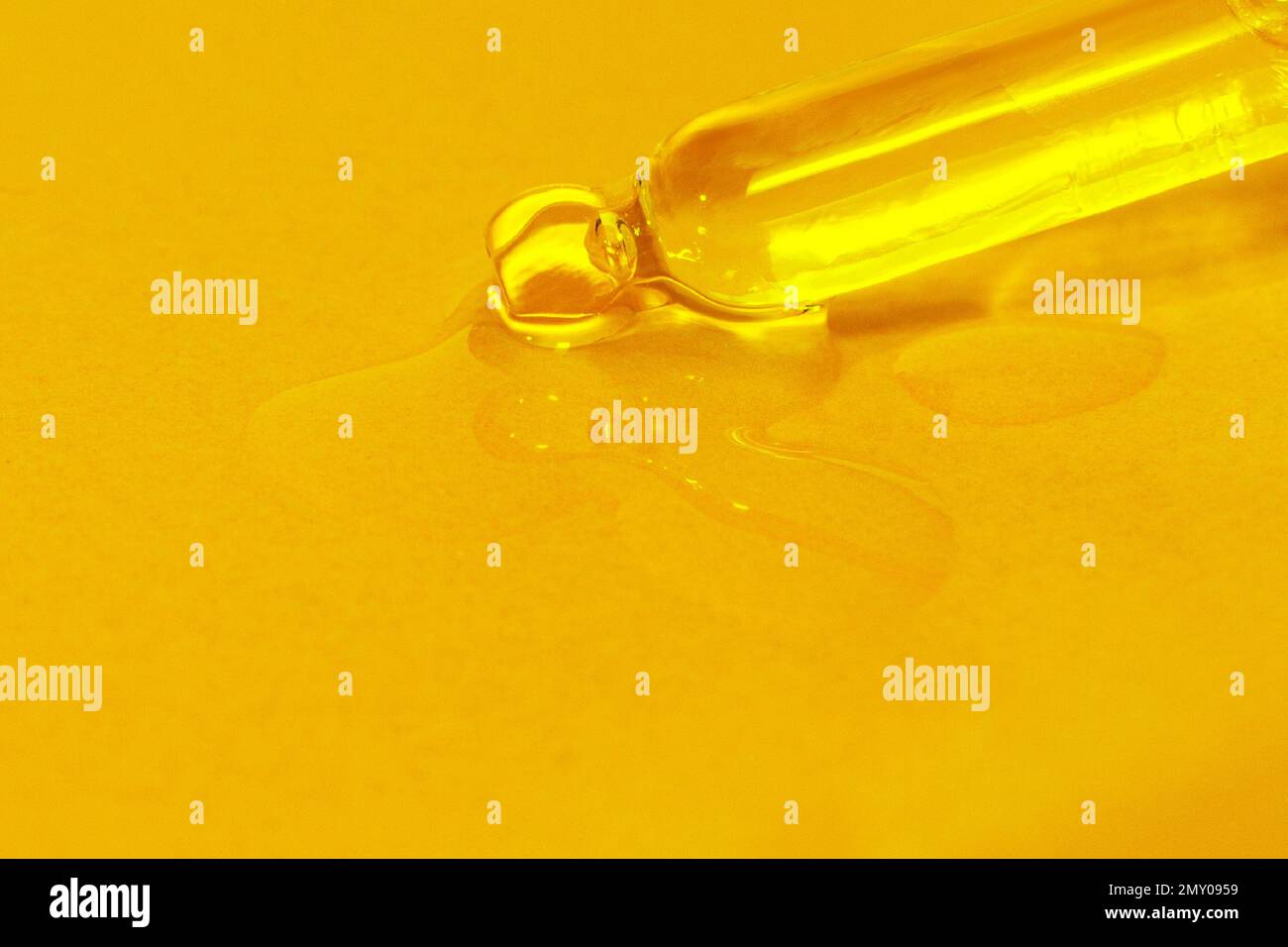 Cosmetic pipette with dripping liquid, oil and drops on a yellow ...