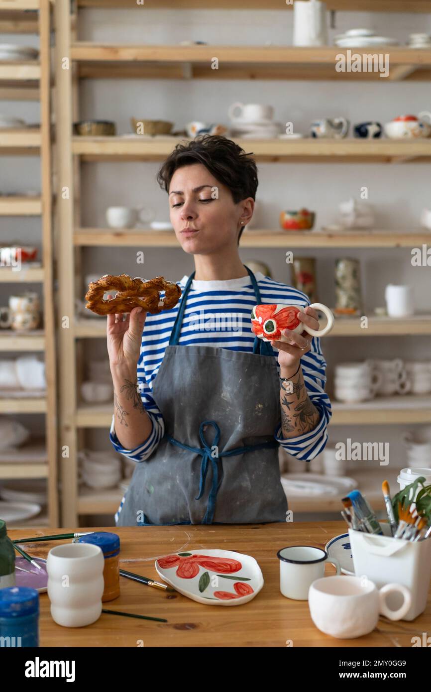 Female ceramic artist eating sweet delicious freshly baked bun and ...