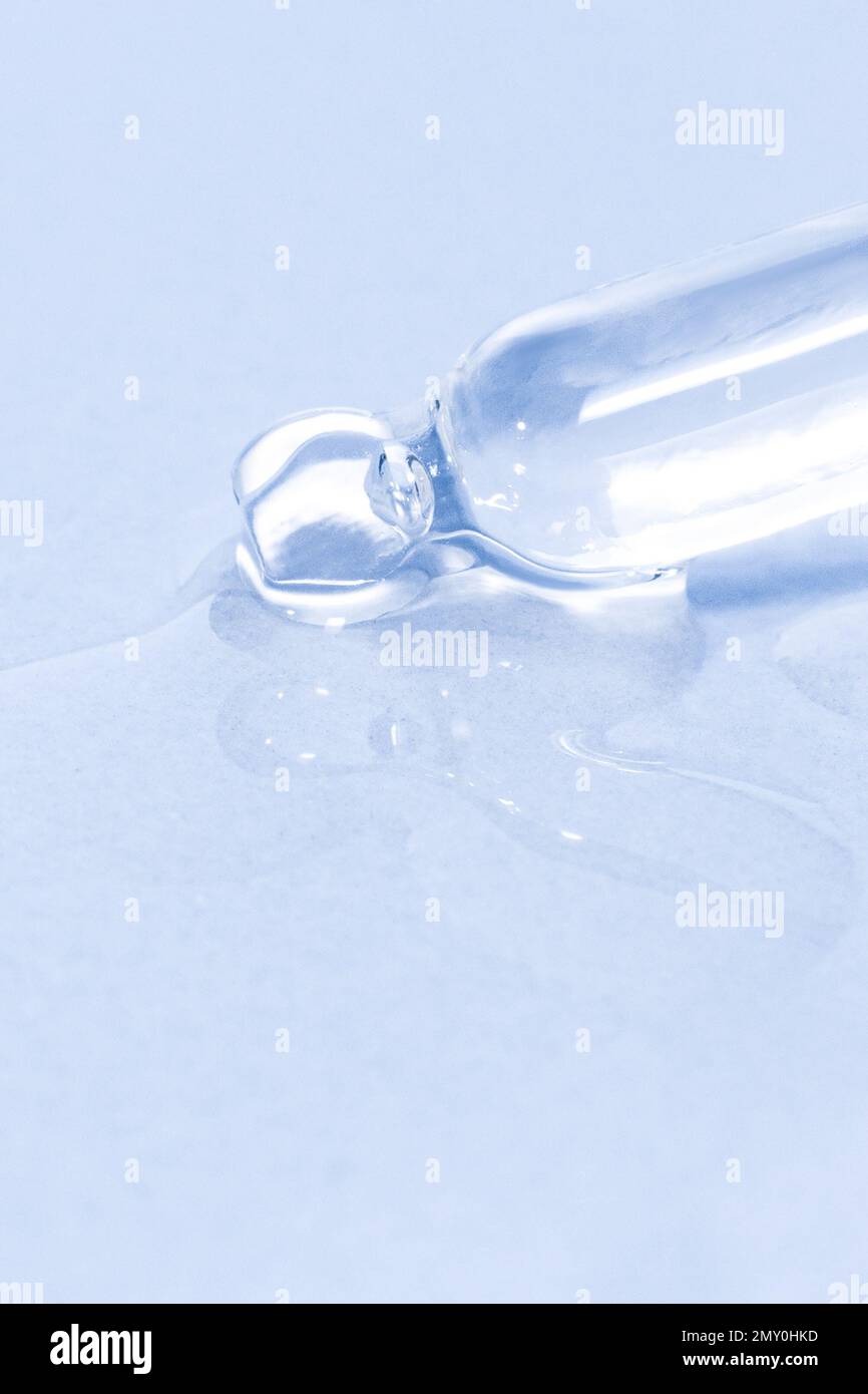 Cosmetic pipette with dripping liquid and drops on a blue background ...