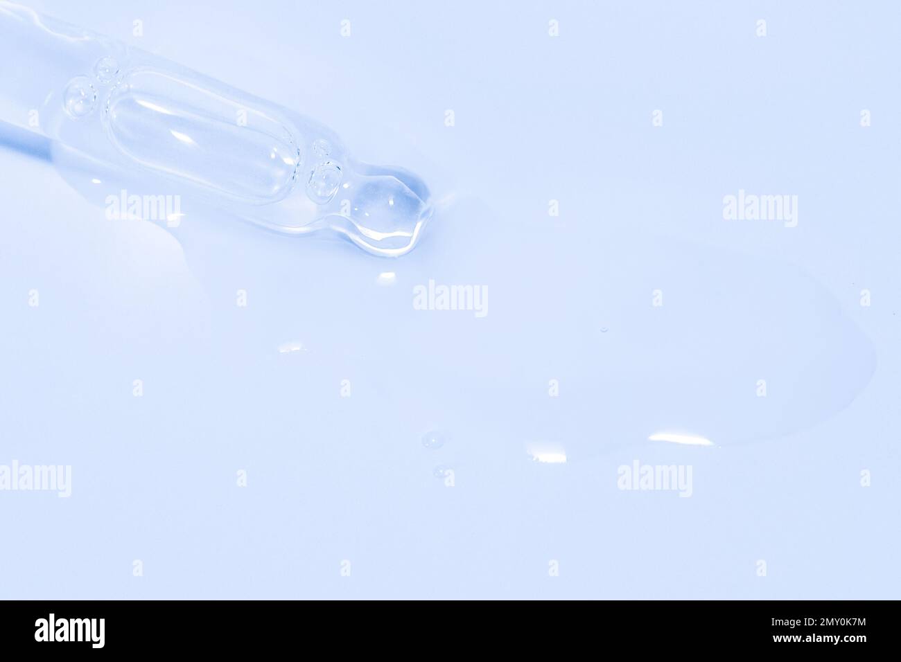 Cosmetic pipette with dripping liquid and drops on a blue background ...