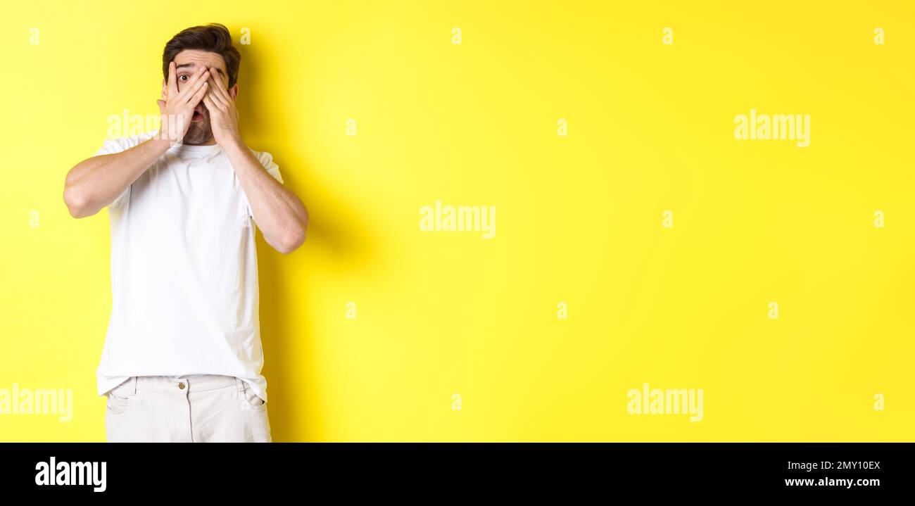 Embarrassed guy shut eyes but peeking through fingers at something ...