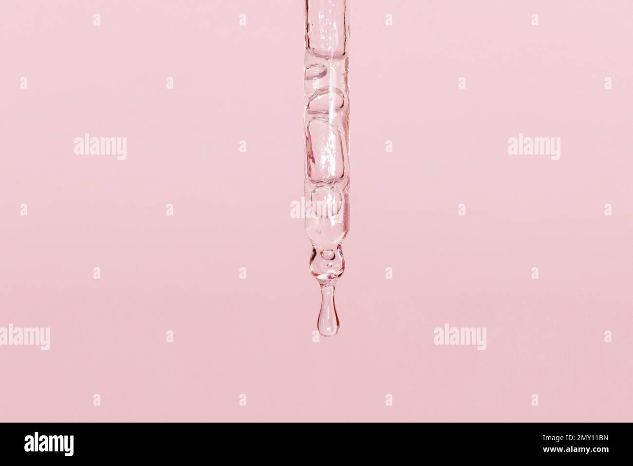 Cosmetic pipette with dripping liquid and drops on a pink background ...