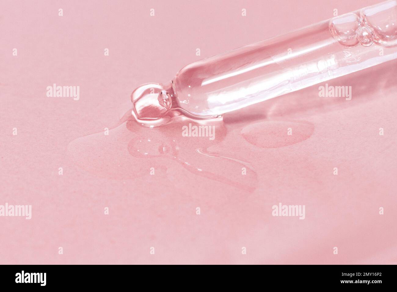 Cosmetic pipette with dripping liquid and drops on a pink background ...