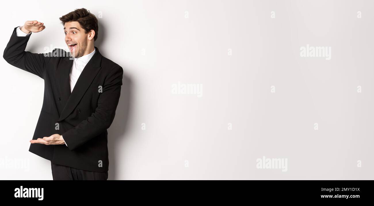 Portrait of excited handsome man in suit, shaping big object on copy ...