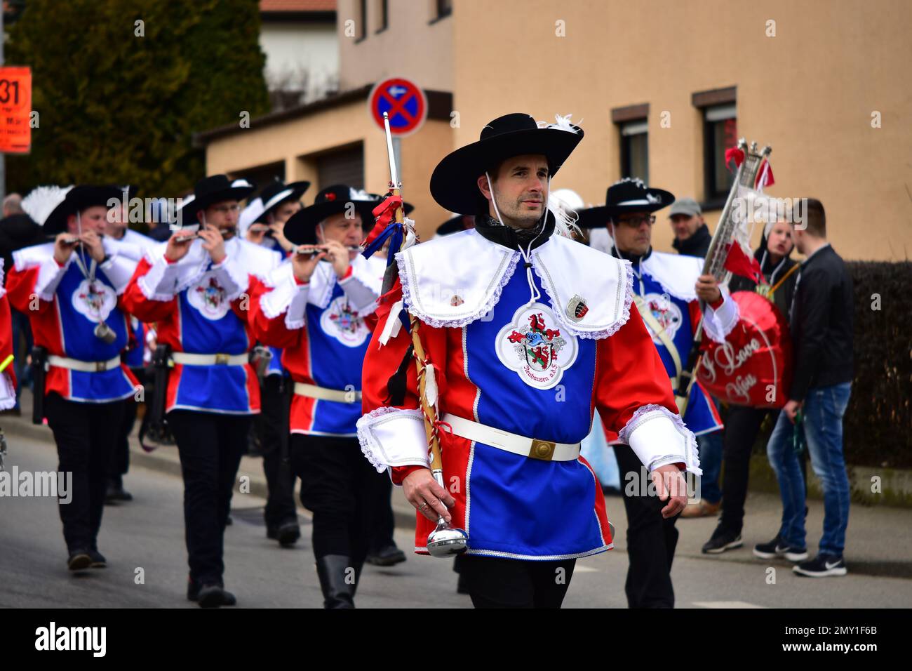 A group of men in blue and red troubadour costumes playing flutes and ...