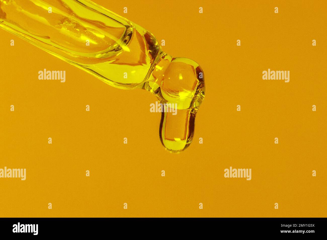 Cosmetic pipette with dripping liquid, oil and drops on a yellow ...