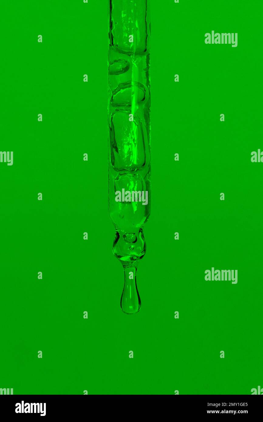 Cosmetic pipette with dripping liquid, oil and drops on a green ...
