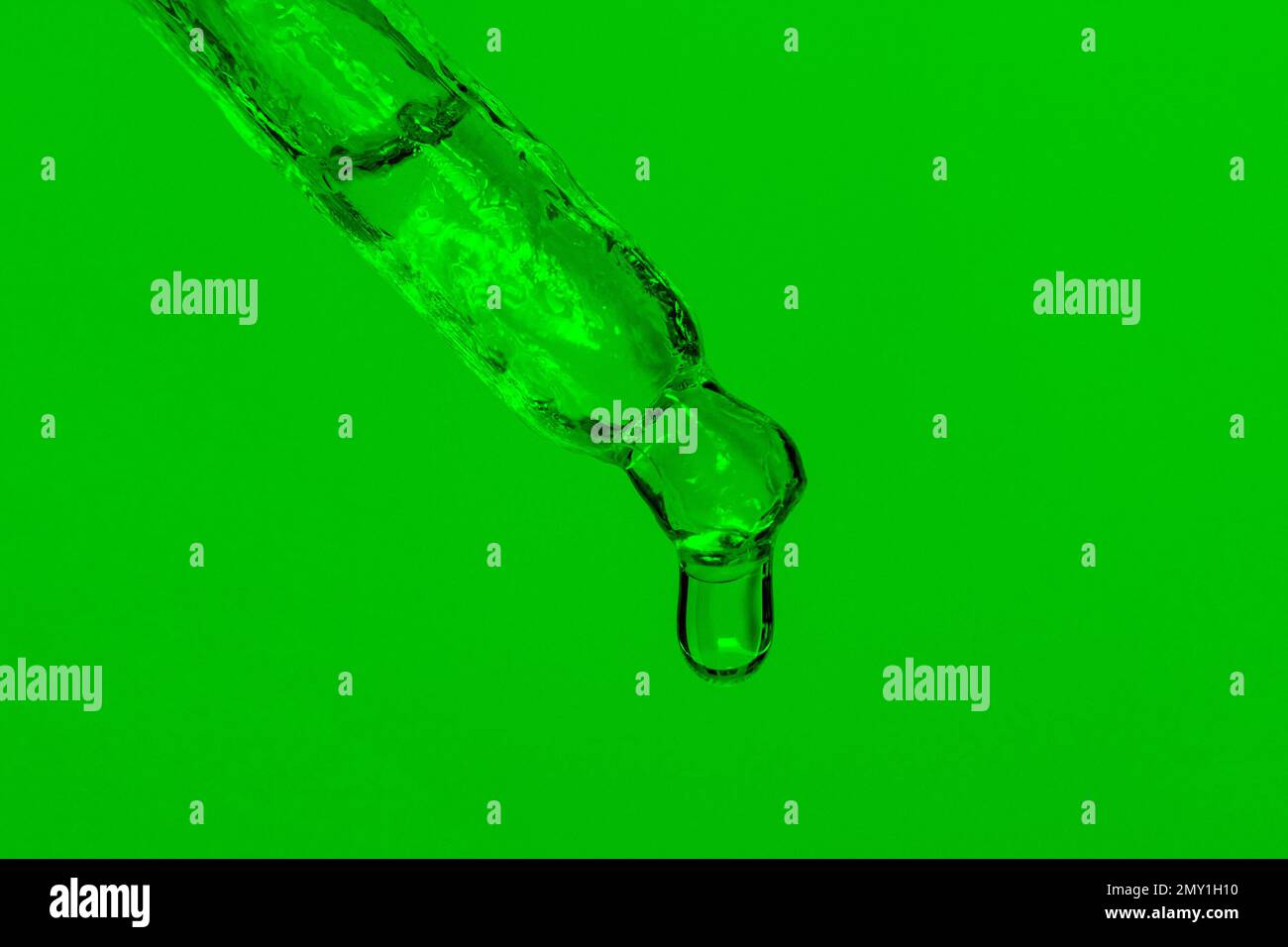 Cosmetic pipette with dripping liquid, oil and drops on a green ...
