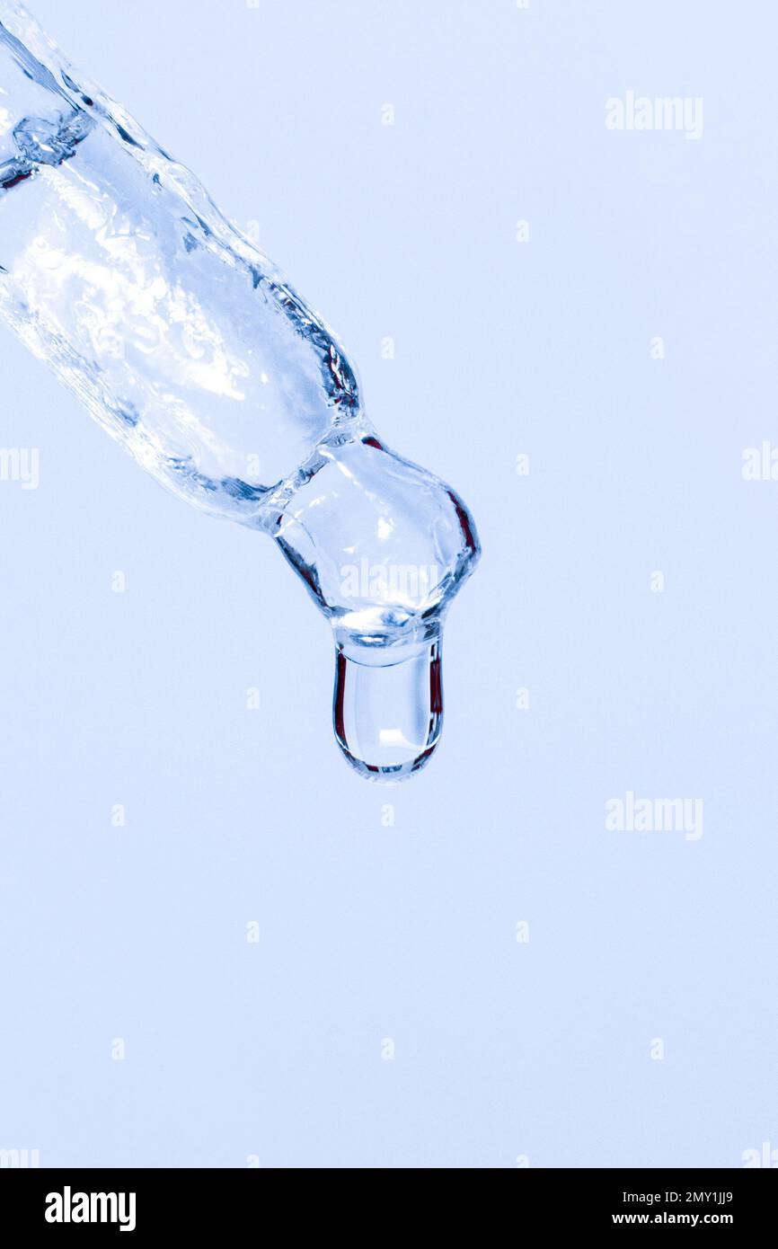 Cosmetic pipette with dripping liquid and drops on a blue background ...