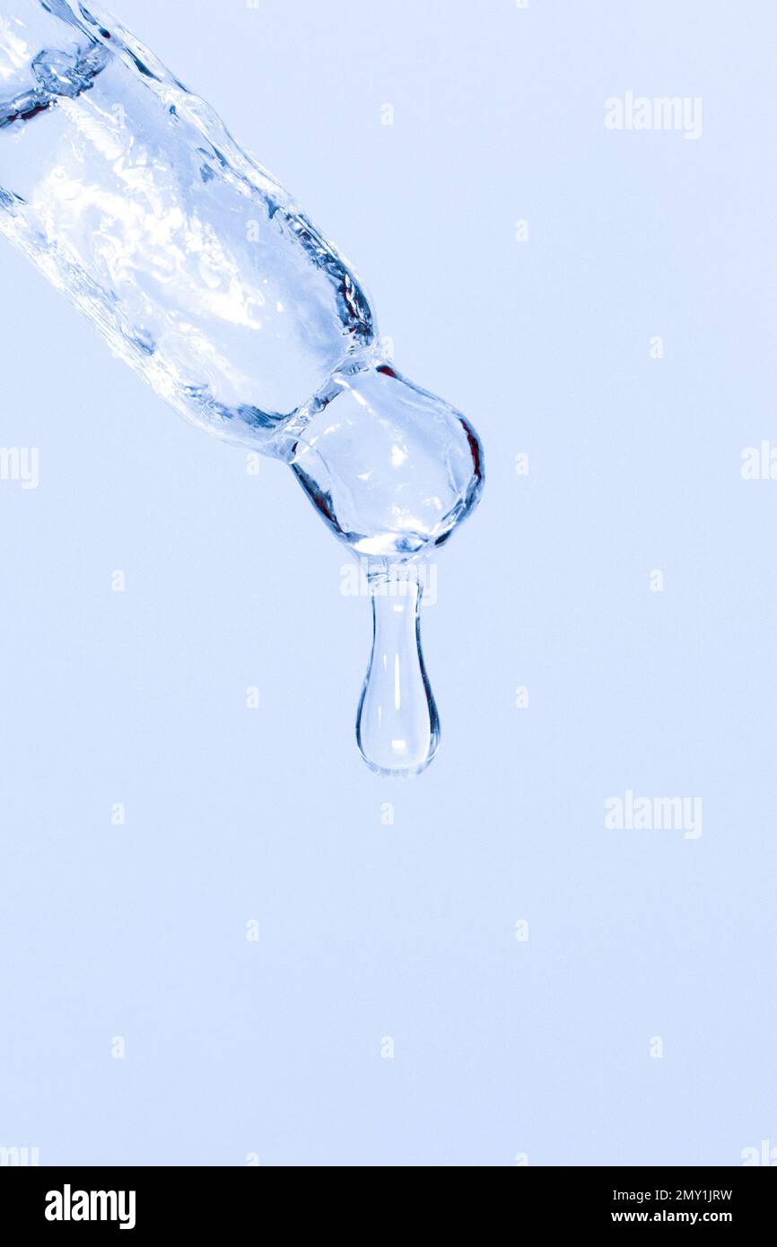 Cosmetic pipette with dripping liquid and drops on a blue background ...
