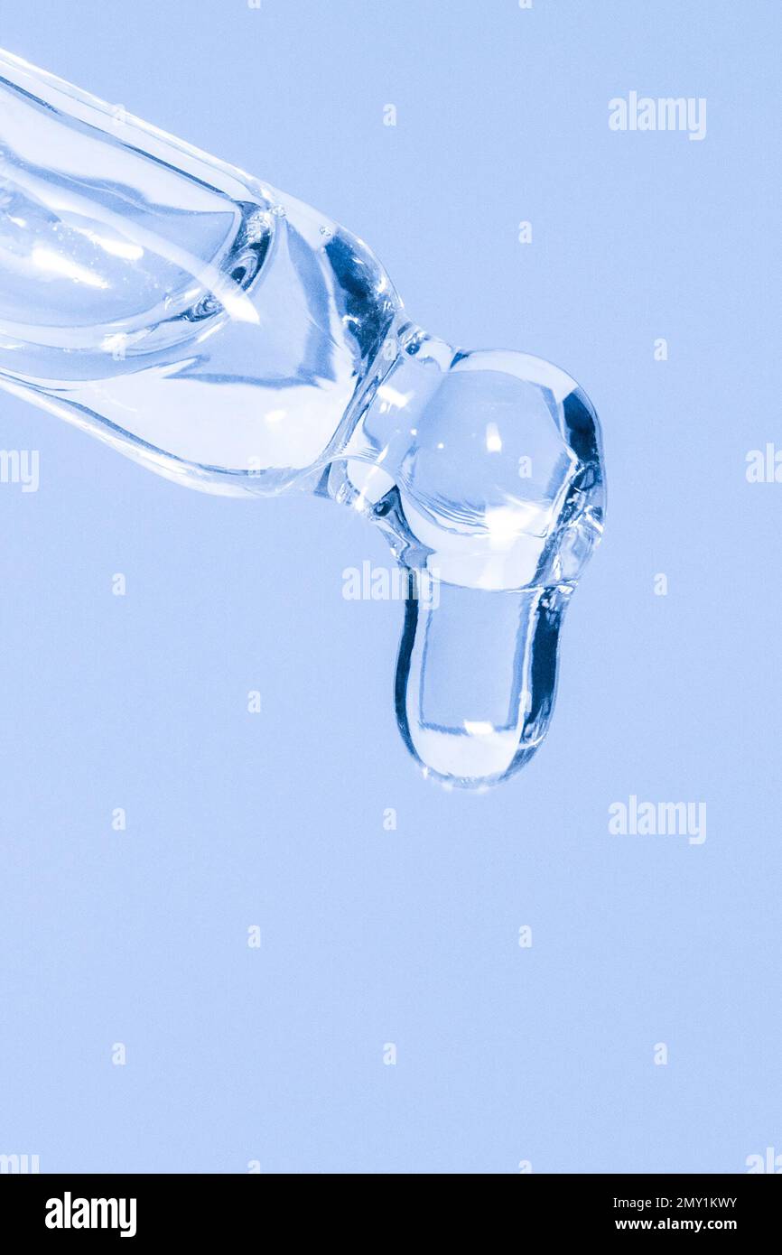 Cosmetic pipette with dripping liquid and drops on a blue background ...