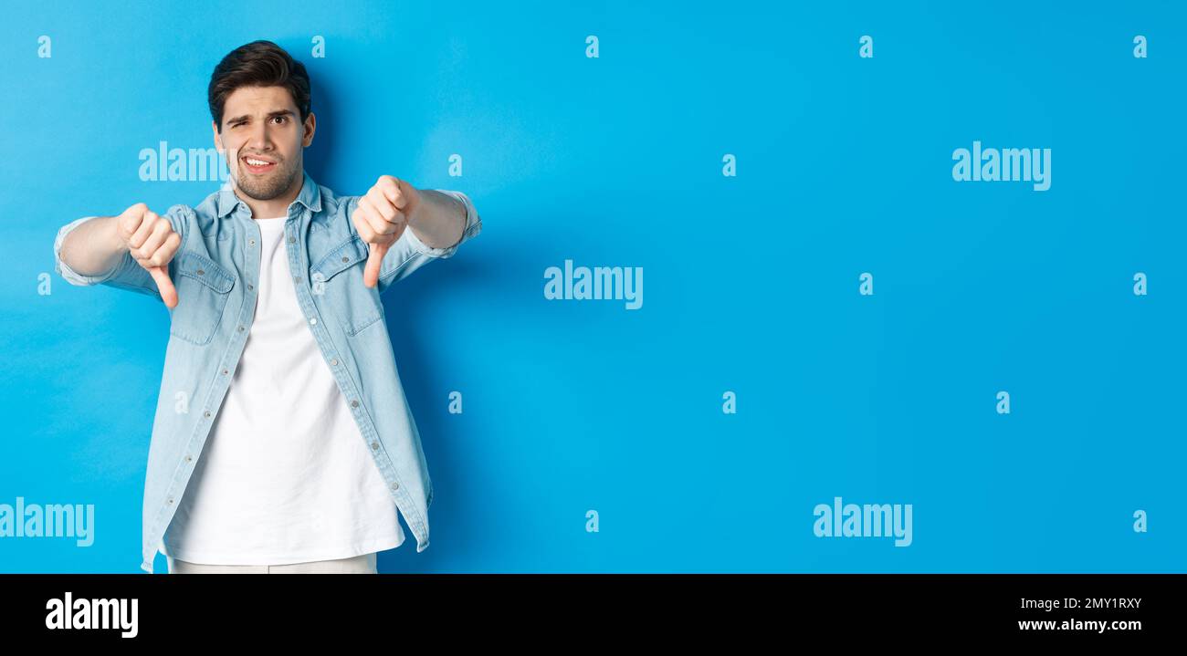 Disappointed man showing thumbs down and grimacing at something awful ...