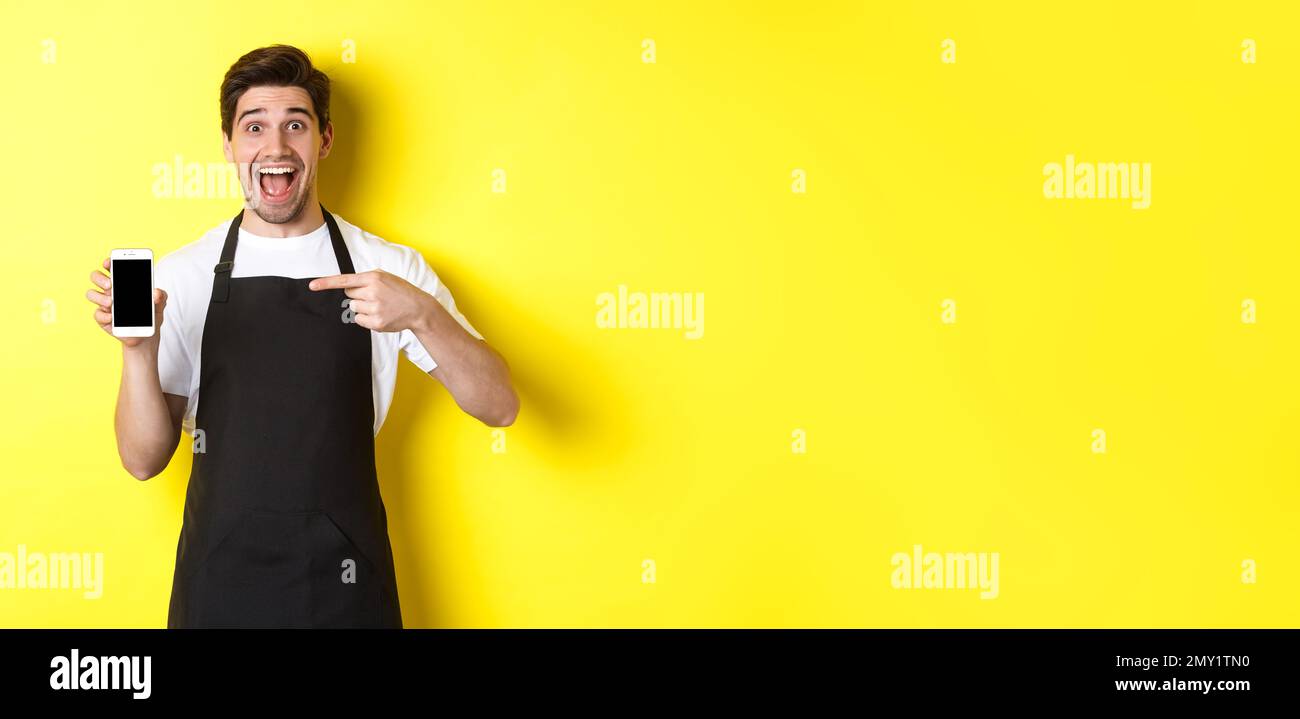 Handsome barista in black apron pointing finger at mobile screen ...