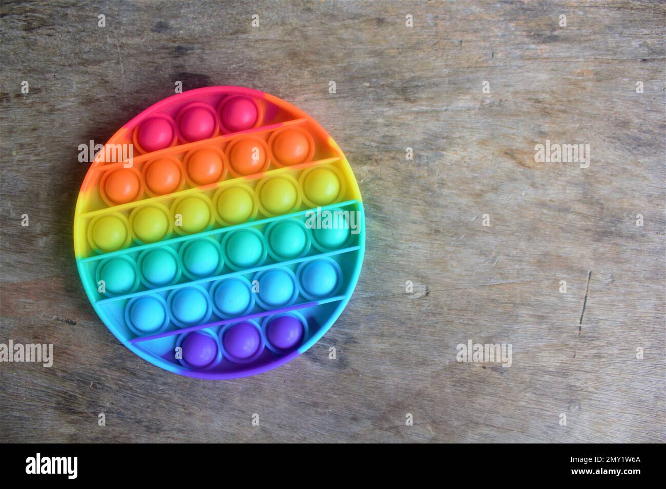 Rainbow colored silicone pop it kids toy on wood texture background ...