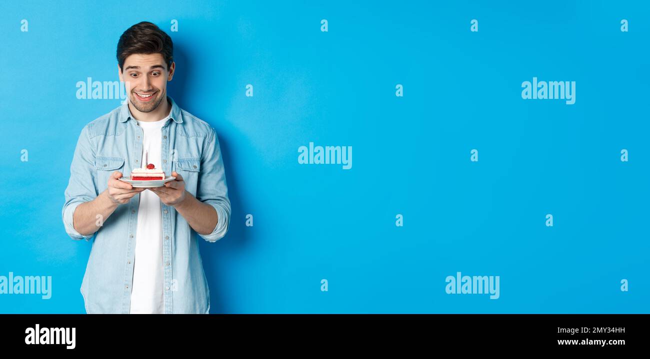 Happy man looking at birthday cake and making with, standing over blue ...