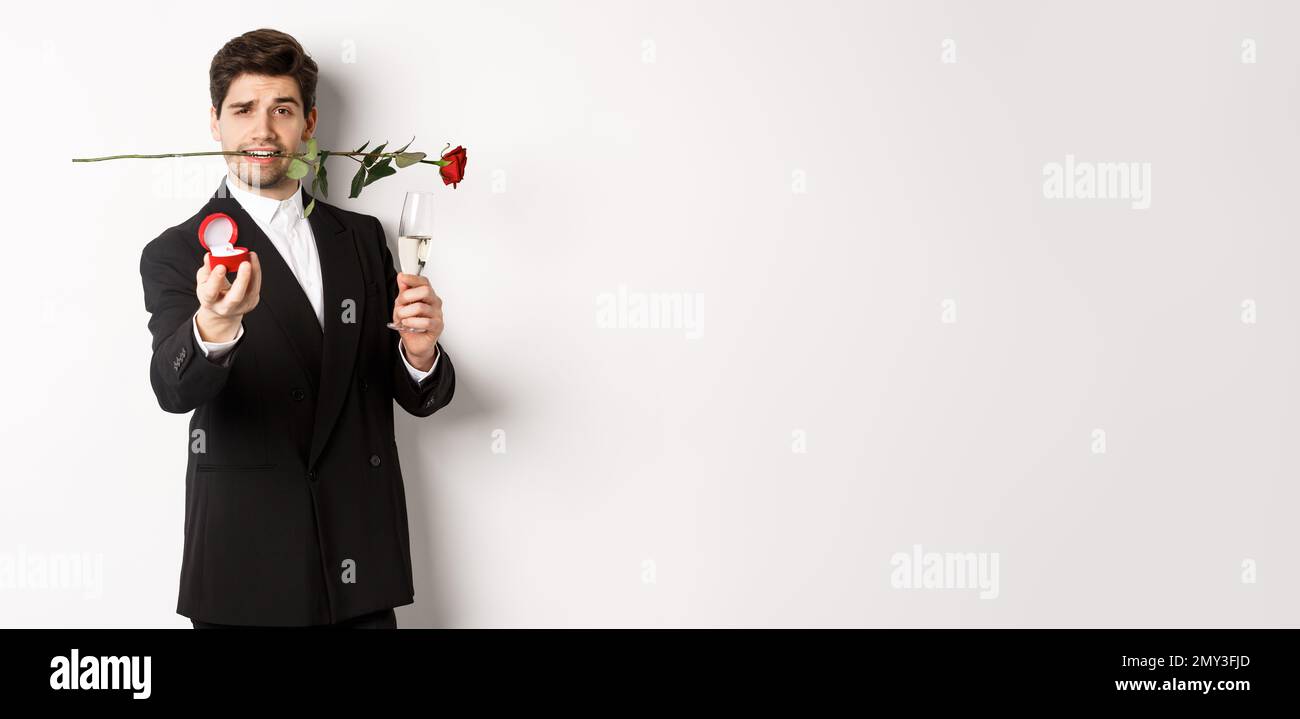 Romantic young man in suit making a proposal, holding rose in teeth and ...
