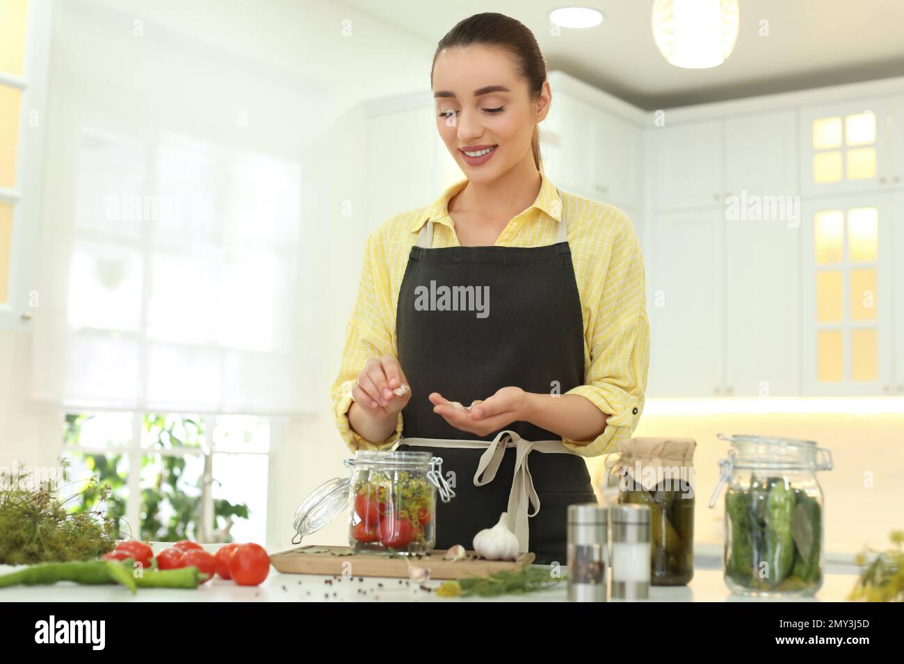 Woman putting garlic into pickling jar at table in kitchen Stock Photo ...