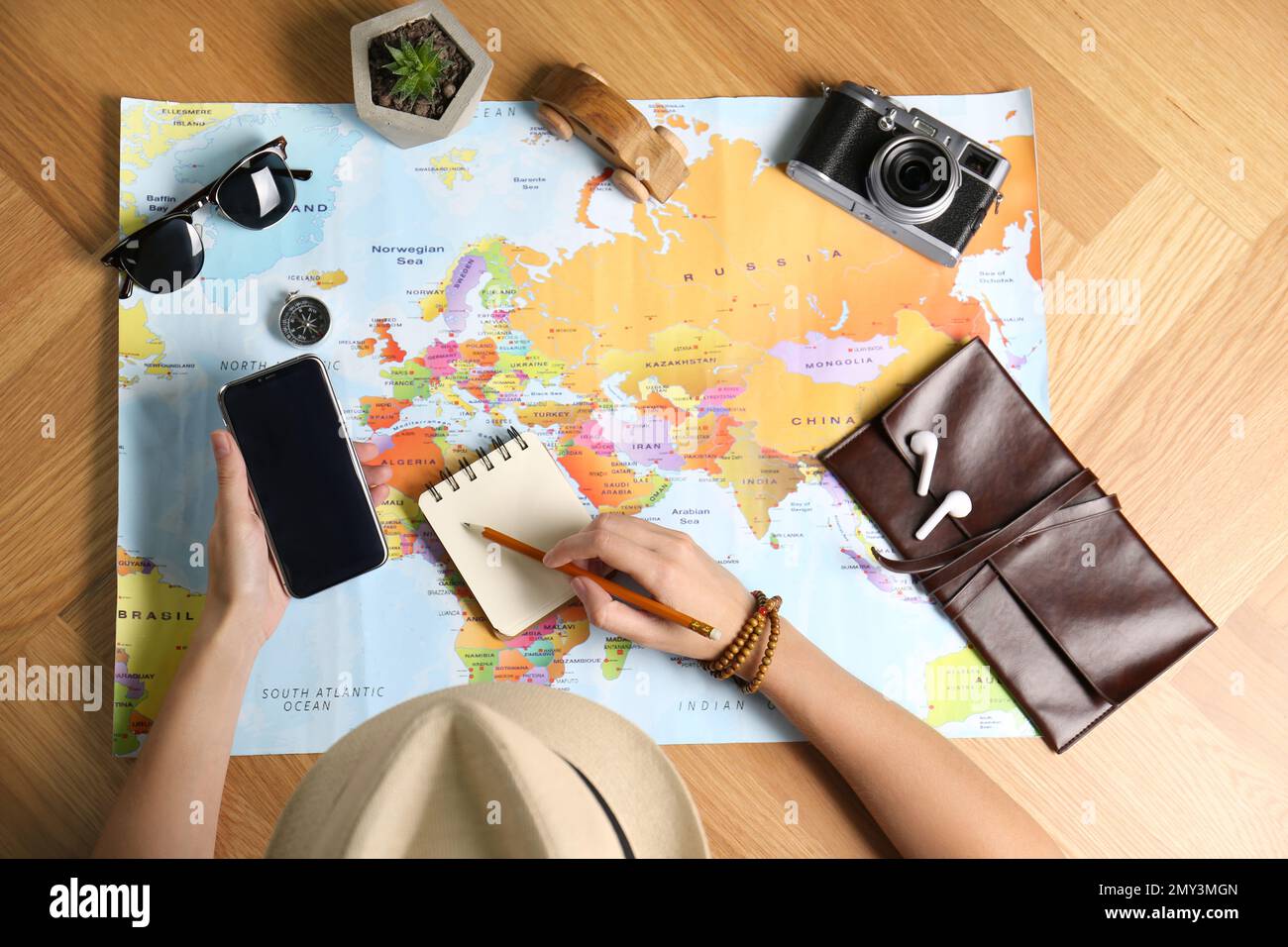 Woman with smartphone and world map planning trip at wooden table, top ...