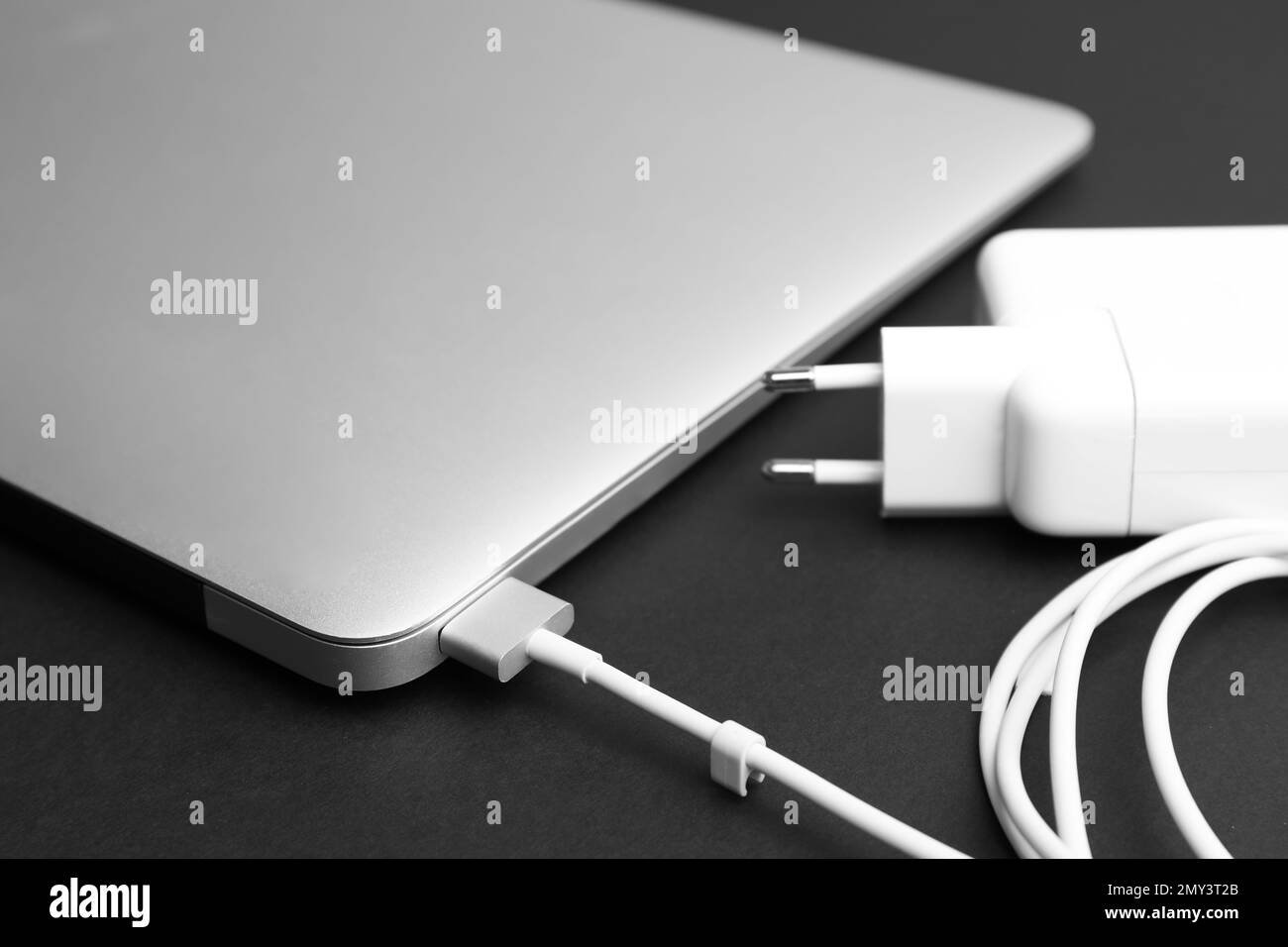 Laptop and charger on black background, closeup. Modern technology ...